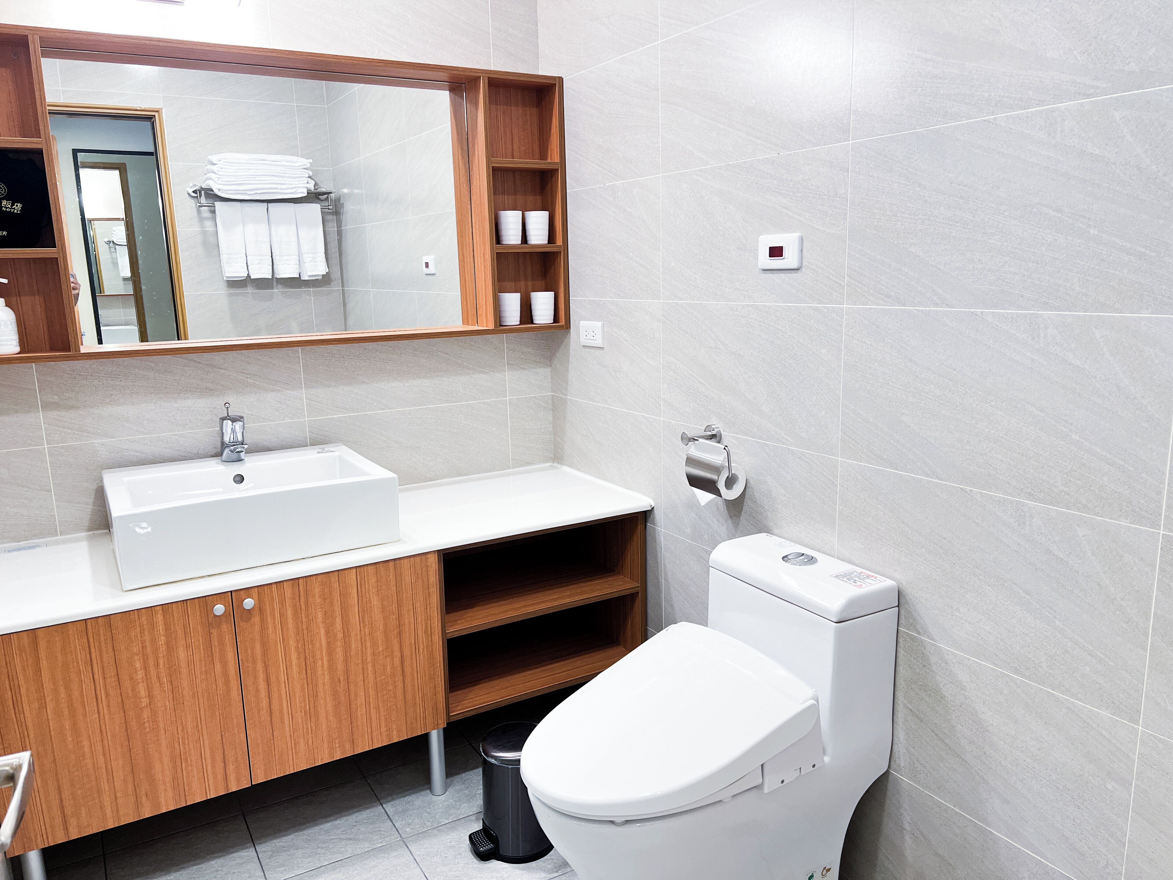 Uma casa de banho moderna com lavatório branco, toucador de madeira e sanita.
