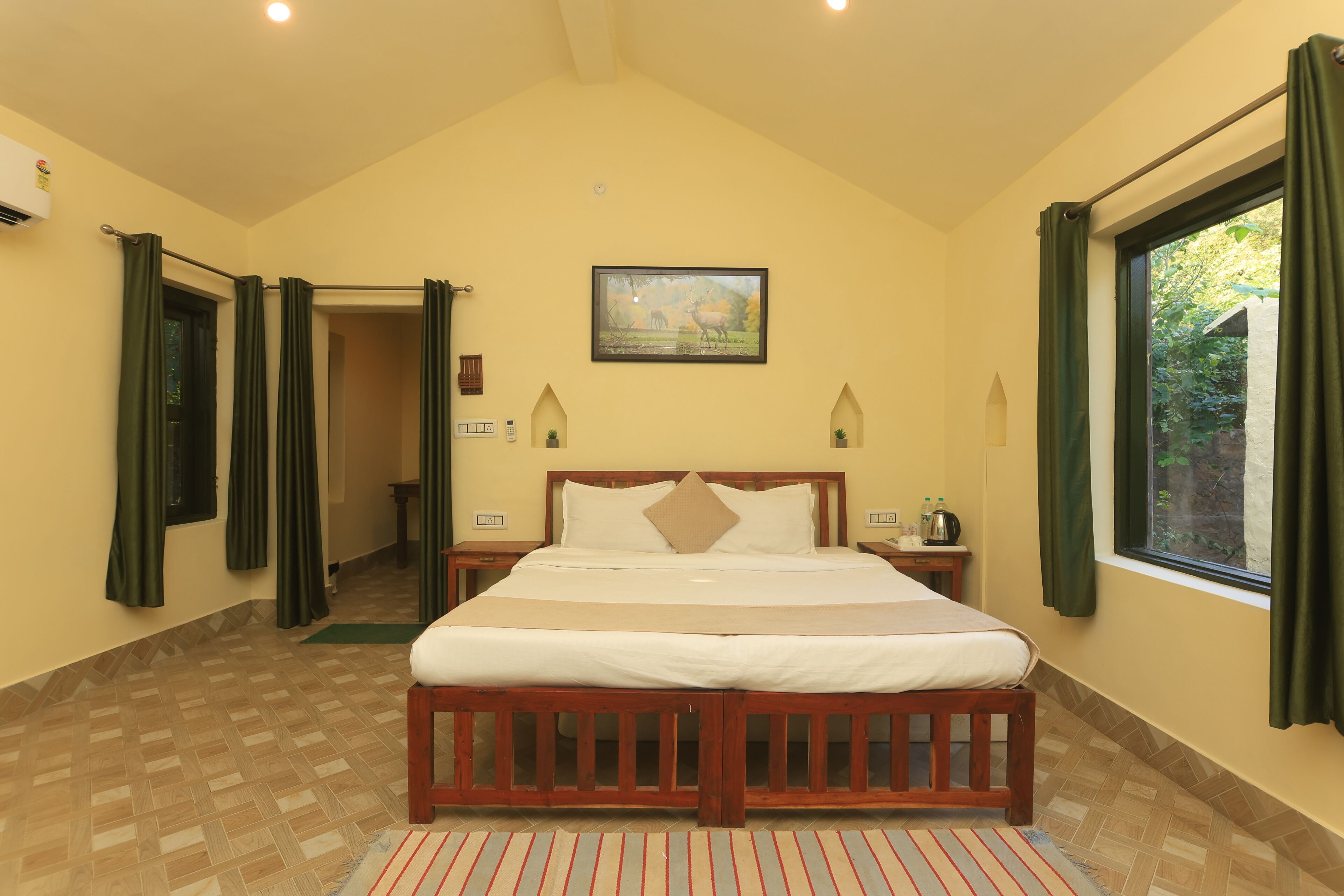 Quarto de hotel com cama de madeira, um quadro na parede e vista para o exterior pela janela.