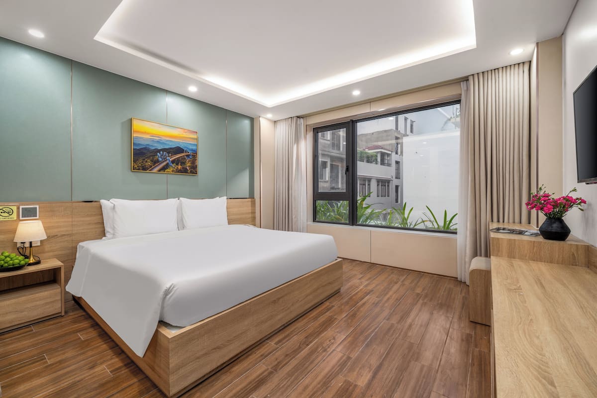Quarto de hotel moderno com uma cama grande, uma escrivaninha, uma televisão e uma janela com vista para a cidade.