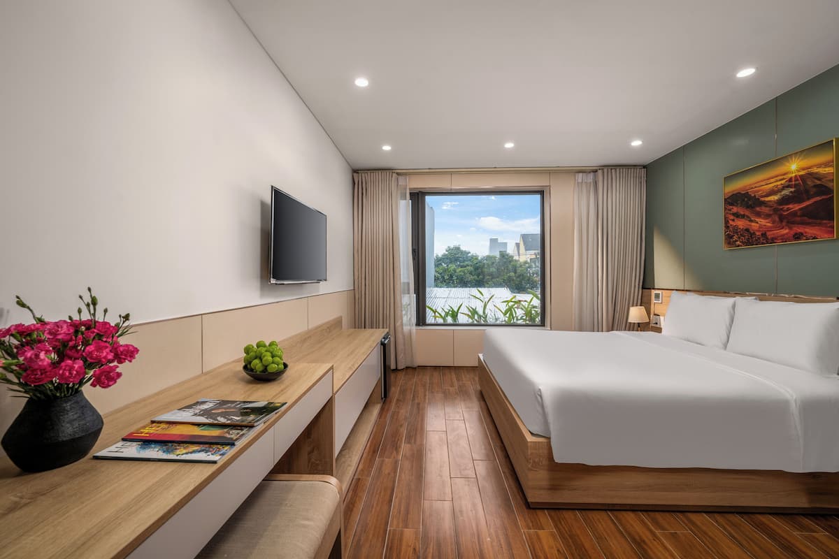 Quarto de hotel moderno com uma cama grande, uma escrivaninha com televisão de tela plana, uma janela com vista para a cidade e um quadro na parede.