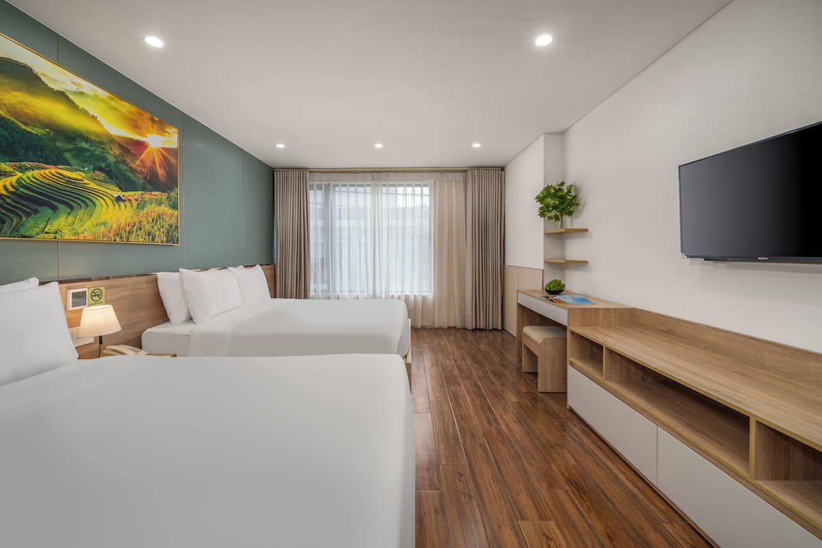 Quarto de hotel com duas camas, televisão, secretária e uma janela grande com cortinas.