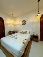 Quarto bem arrumado com uma cama grande, duas mesas de cabeceira, um espelho e duas luminárias pendentes.
