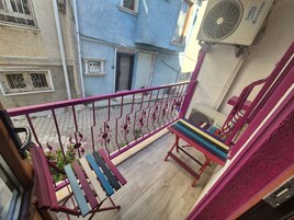 Uma varanda com piso de madeira, grade de metal e um banco colorido.