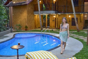 Piscina com deck de madeira, uma espreguiçadeira e uma mesa com um copo de bebida.