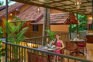 Uma área de refeições com uma mesa posta para dois, rodeada por cadeiras de vime, com vista para edifícios tradicionais ao fundo.