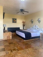 Quarto com cama, ventilador de teto, pintura e vaso com plantas.