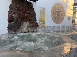 Uma área de spa com uma nascente termal, parede de pedra e cartazes informativos.