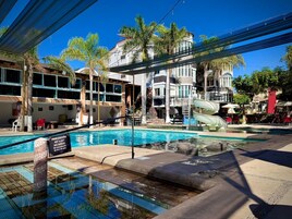 Uma área de piscina com escorregador, palmeiras e um edifício com várias varandas.