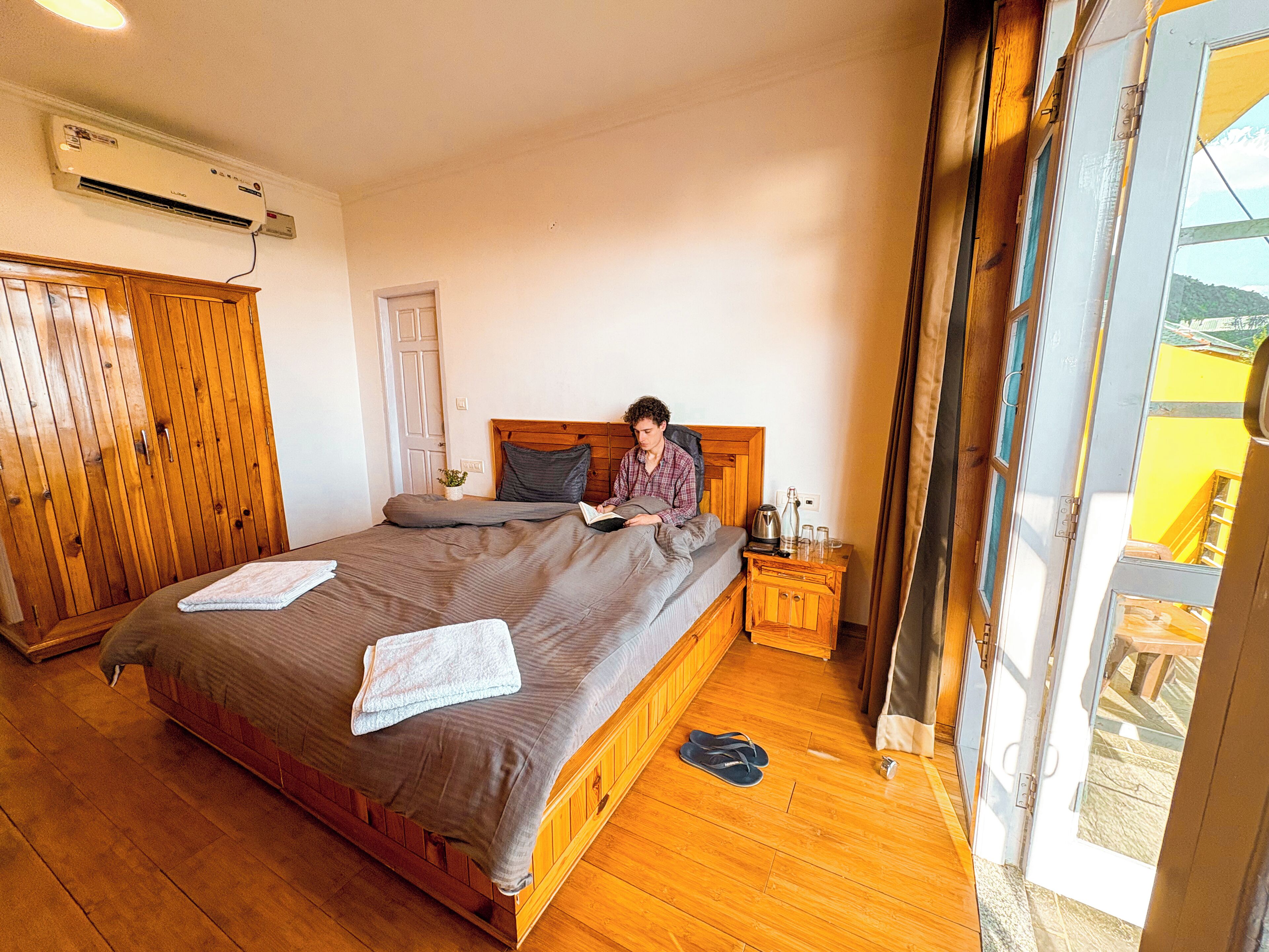 Quarto com cama de madeira, mesa de cabeceira, janela com cortinas e vista para o exterior.