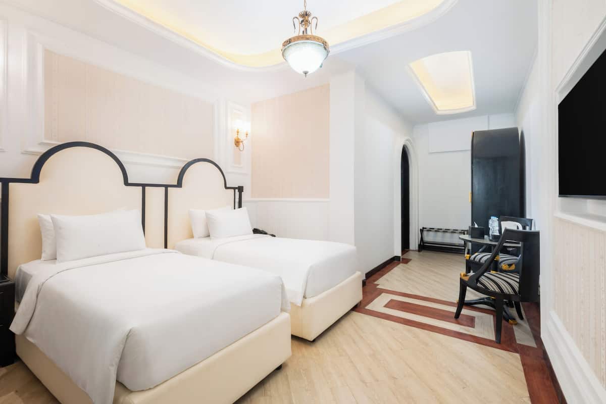 Quarto de hotel com duas camas, uma escrivaninha, uma cadeira e uma televisão.