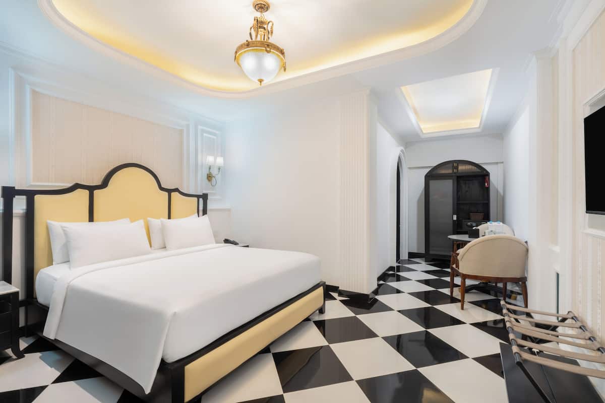 Quarto de hotel com cama grande, escrivaninha, cadeira, televisão e banheiro com espelho e pia.