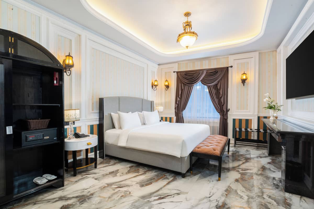 Quarto de hotel com uma cama grande, uma escrivaninha, uma televisão e um guarda-roupa.
