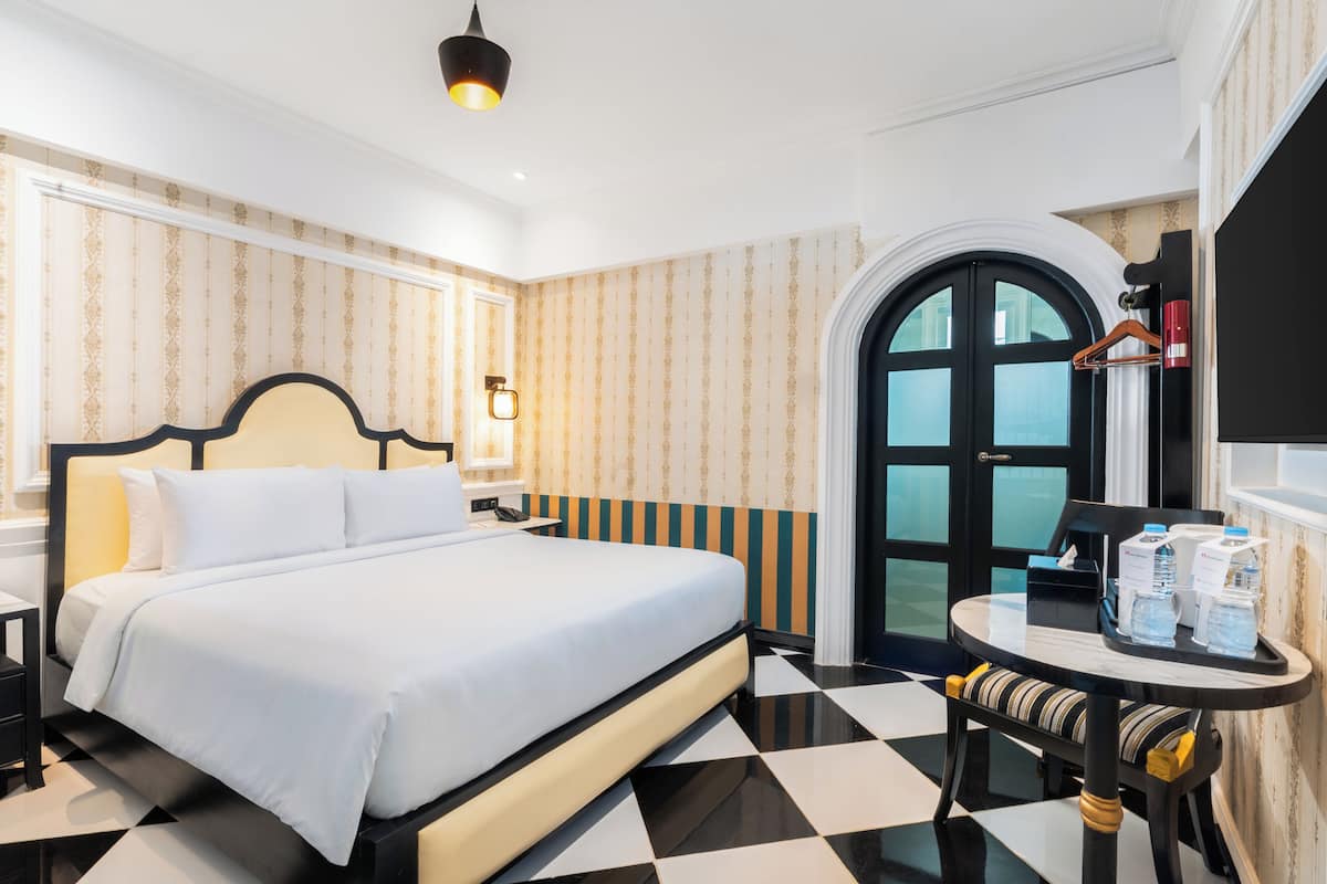 Quarto de hotel com uma cama, uma mesa redonda com uma cadeira, uma escrivaninha, um telefone e uma porta com vista.