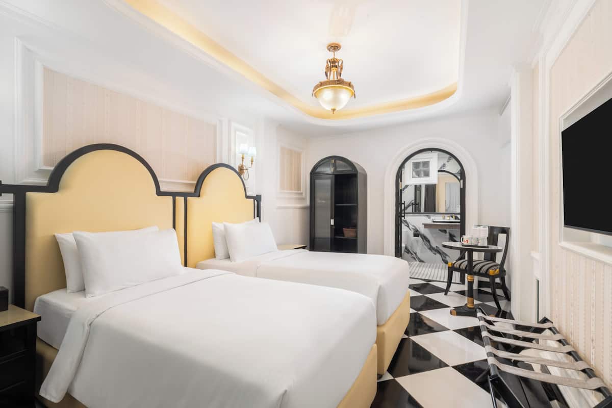 Quarto de hotel com duas camas, área de refeições, televisão e banheiro com espelho.