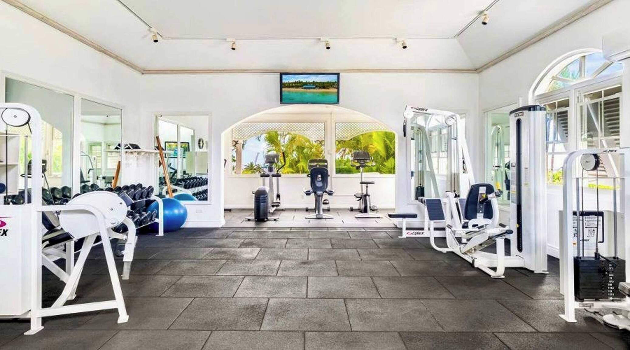 Uma academia com diversos equipamentos de exercício, incluindo halteres, uma bicicleta ergométrica e um remo.