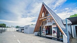 Um edifício moderno com telhado inclinado, grandes janelas e área de estacionamento com carros.