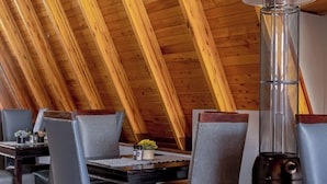 Uma sala de jantar com vigas de madeira, mesas, cadeiras e um aquecedor central.