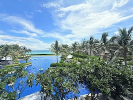 Piscina de resort com vista para o oceano, cercada por palmeiras e vegetação.