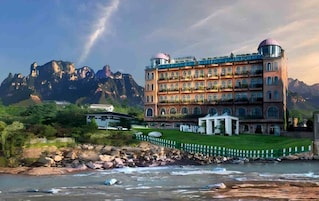 Um hotel com um edifício grande, uma ponte e montanhas ao fundo.