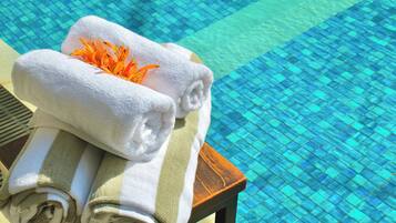 Um ambiente junto à piscina com toalhas e uma flor.