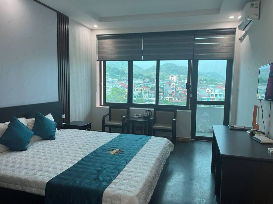 Quarto de hotel com uma cama grande, duas cadeiras, uma escrivaninha e uma televisão.