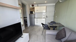 Uma sala de estar moderna com televisão de tela plana, sofá cinza e um espaço de jantar com mesa e cadeiras.