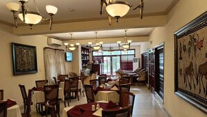 Uma sala de jantar com várias mesas e cadeiras, um candelabro e obras de arte nas paredes.