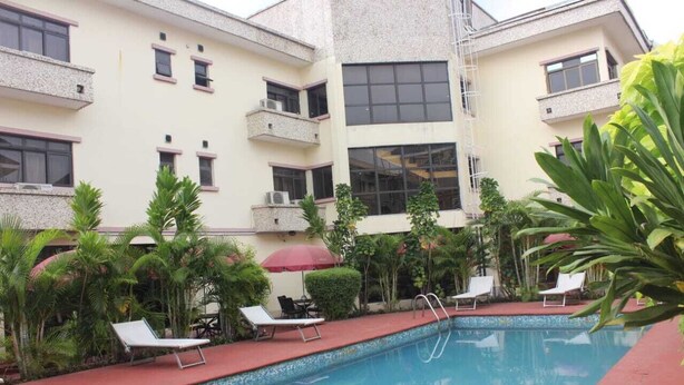Área de piscina com espreguiçadeiras e guarda-sóis, rodeada por um edifício com varandas e janelas.