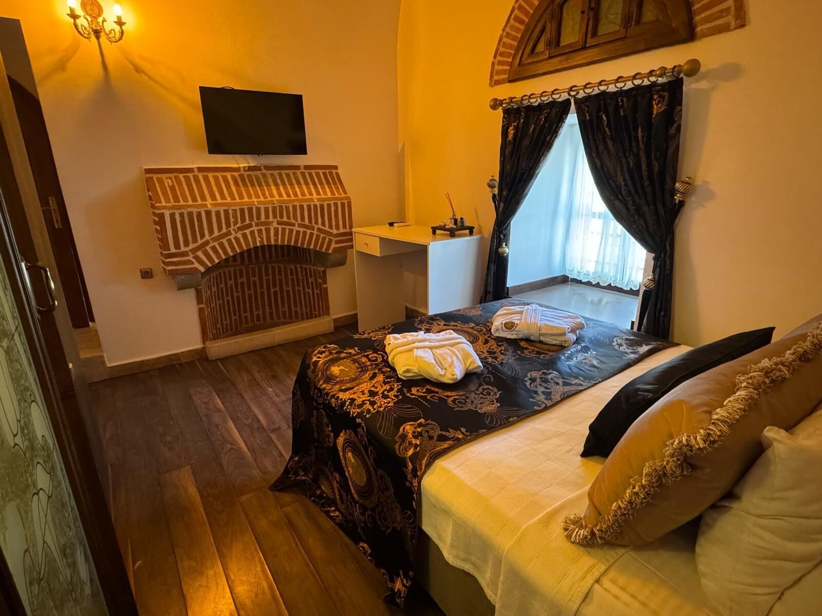 Quarto de hotel com lareira, cama com toalhas, televisão e janela com cortinas.