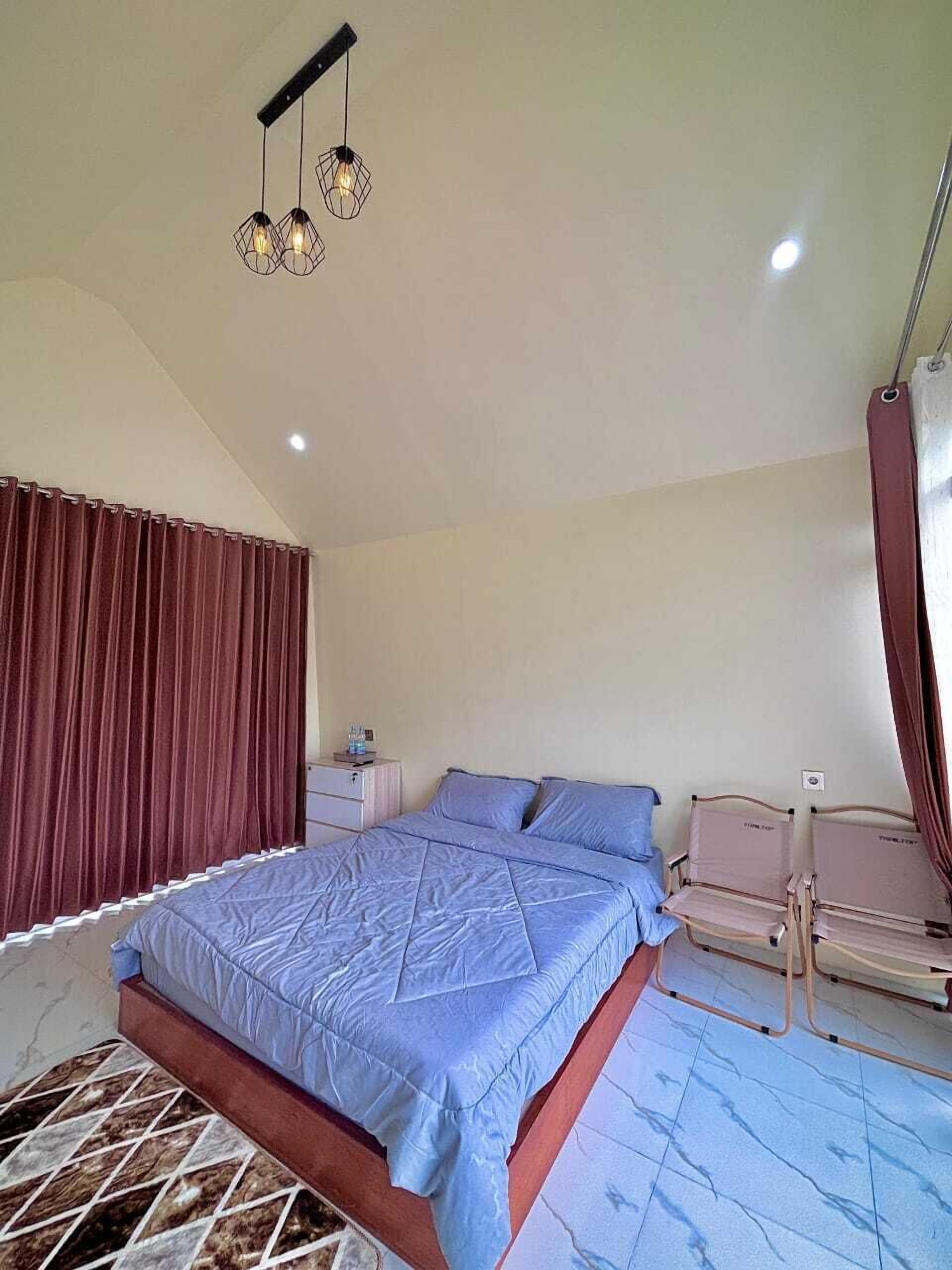 Quarto com cama, mesa de cabeceira, cadeira e luminária pendente.