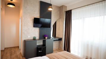 Quarto moderno com cama, escrivaninha, televisão e janela com cortinas.
