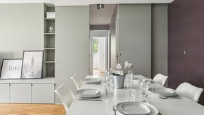 Uma sala de jantar moderna com uma mesa comprida posta para seis pessoas, cadeiras brancas e decoração minimalista.
