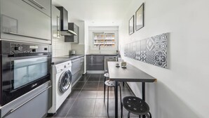Cozinha compacta com eletrodomésticos modernos, área de refeições com banquetas e azulejos estampados nas paredes.