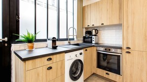 Cozinha compacta com armários de madeira, máquina de lavar, forno e cafeteira.