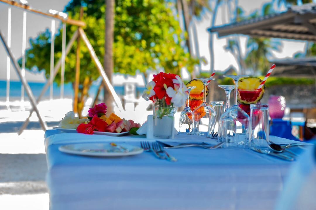 Uma mesa posta com toalha azul, copos transparentes e uma variedade de frutas e flores.