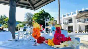 Uma mesa posta com uma bebida tropical, frutas e um copo.