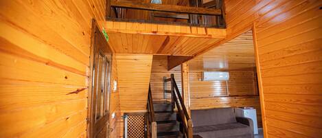Interior de uma cabana de madeira com escada que leva a um mezanino, um sofá e uma pequena mesa.