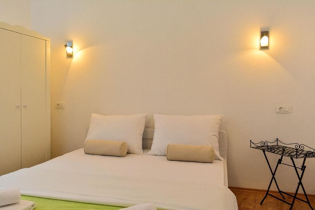 Quarto com cama, duas mesas de cabeceira, guarda-roupa e luzes fixadas na parede.