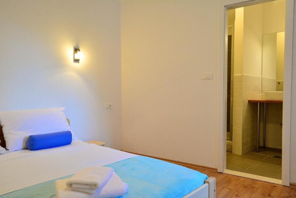Quarto de hotel com cama, mesa de cabeceira, luminária na parede e banheiro visível por uma porta aberta.