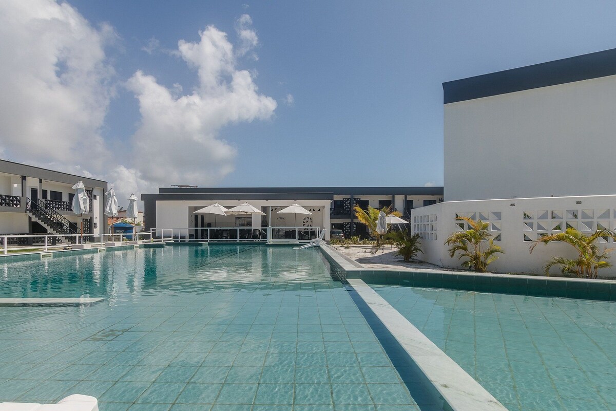 Piscina com água azul cristalina, rodeada por um edifício branco com várias janelas e uma varanda.