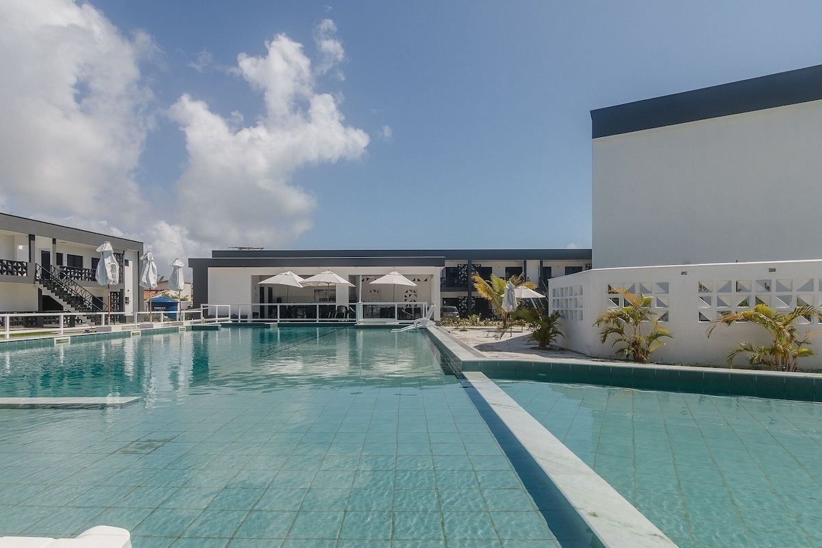 Piscina com água azul cristalina, rodeada por um edifício branco com várias janelas e uma varanda.