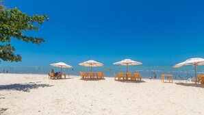 Uma praia com fileiras de cadeiras amarelas e guarda-sóis brancos, céu azul límpido e o oceano ao fundo.