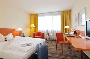 Quarto de hotel com cama, escrivaninha, cadeira e televisão.