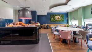 Restaurante moderno com um balcão preto central, assentos ao redor de uma mesa redonda e uma parede verde com planta e letreiro neon.