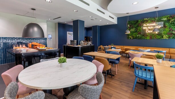 Um restaurante moderno com área de bar, disposição de mesas e um letreiro de neon na parede.