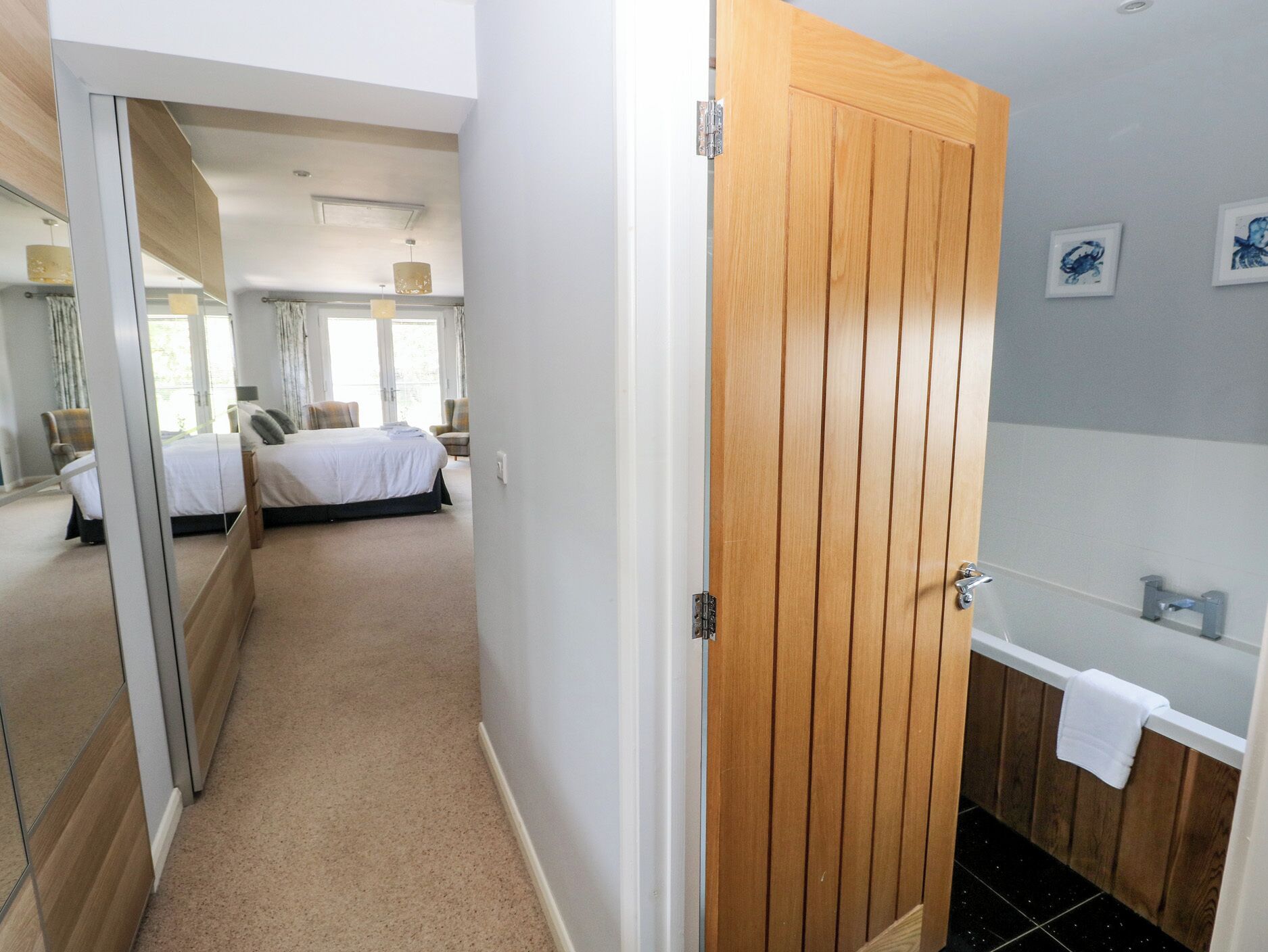 Quarto de hotel com porta de madeira, cama, banheiro com banheira e uma janela grande.