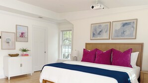 Quarto com uma cama grande, um guarda-roupa branco, uma janela e duas pinturas abstratas na parede.