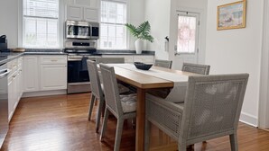 Uma cozinha moderna com armários brancos, eletrodomésticos de aço inoxidável e uma área de refeições com cadeiras de vime e mesa de madeira.