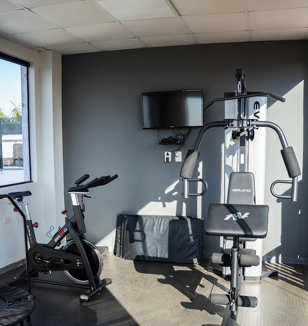Uma academia com equipamentos de ginástica, uma televisão na parede e uma janela que oferece luz natural.