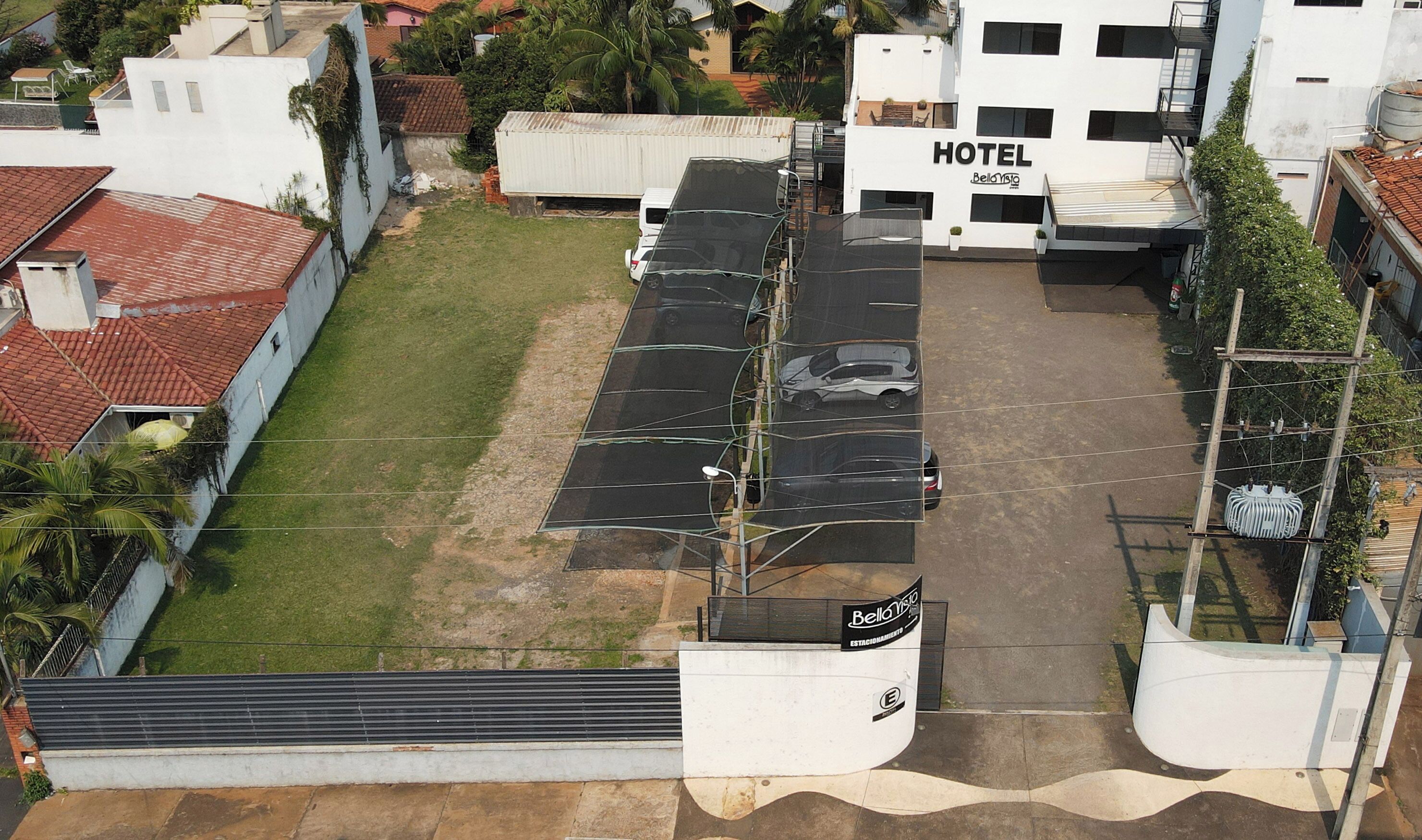 Vista aérea de um hotel com estacionamento, área cercada e edifício com placa indicando ser um hotel.